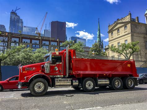 A Red Dump Truck Driving Down A Street Next To Tall Buildings Photo