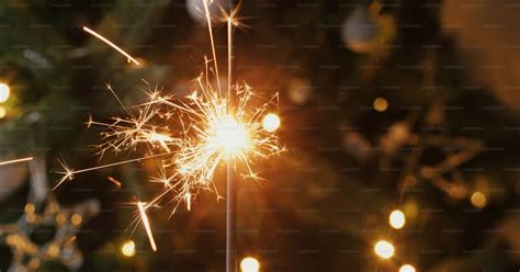 축제 저녁 방에서 크리스마스 트리 조명을 배경으로 불타는 폭죽을 들고 있습니다 새해 복 많이 받으세요 여자 손에 빛나는 불꽃놀이 벵골 텍스트를 위한 공간입니다 대기