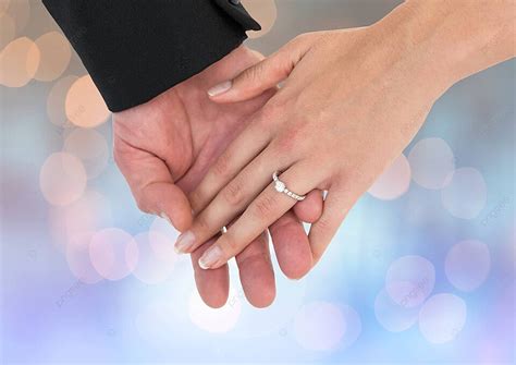 أيدي متشابكة تعرض خاتم الخطوبة للزفاف على خلفية متلألئة من أضواء