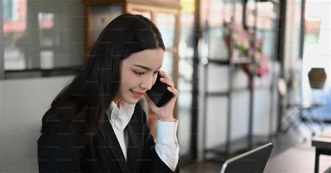 검은 양복을 입은 젊은 아름다운 여성이 사무실에 앉아 휴대폰으로 이야기하고 태블릿을 사용하고 있다 사진 Unsplash의 태국 이미지