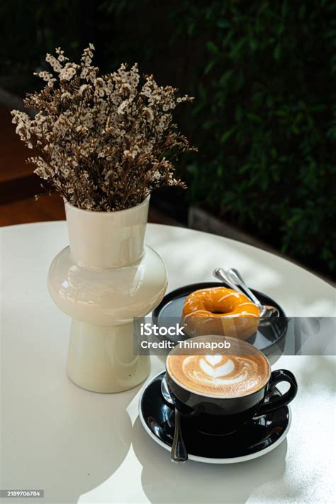 라떼 아트 컵 머그잔에 담긴 우유 거품을 곁들인 뜨거운 커피 라떼 수제 오렌지 도넛 나무 책상 나무 책상이 보입니다 아침 식사로 카페의 커피 숍에서 비즈니스 작업 컨셉 0