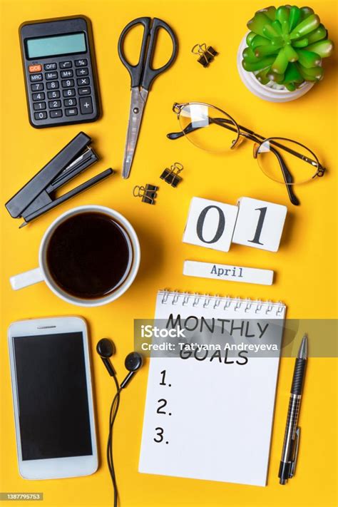 커피 컵 안경 문구류 계산기 및 식물이있는 사무실 작업장 4월 01일 흰색 메모장 페이지에 월별 목표를 텍스트로 설정합니다 테이블 데스크 상단 보기 플랫 레이 1에 대한