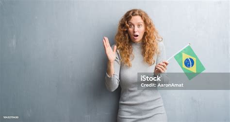 그런 지 회색 벽 지주에 젊은 빨강 머리 여자 브라질 매우 행복 하 고 흥분 상자 식 축 하 승리 큰 웃음과 비명과 손을의 깃발 곱슬 머리에 대한 스톡 사진 및 기타 이미지