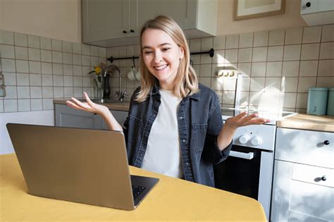 어린 금발 소녀는 미소를 지으며 부엌에서 노트북을 들고 앉아 집에서 일합니다 원격 근무의 개념 주부의 삶 20 29세에 대한