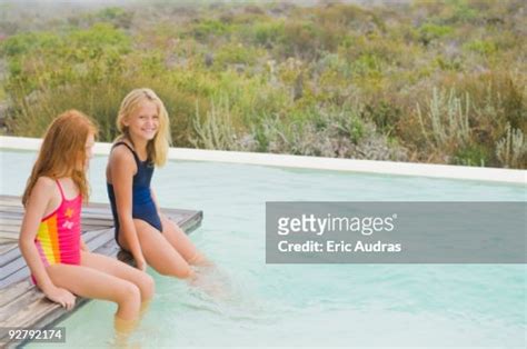 Two Girls Sitting On A Platform At An Infinity Pool High Res Stock