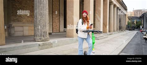 Redhead Girl Tourist With Backpack Uses Mobile Phone To Rent E Scooter On Streets Of European