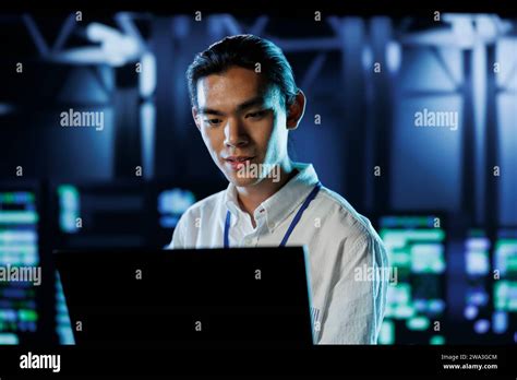 Asian Man Between Server Hub Rows Providing Processing Resources For