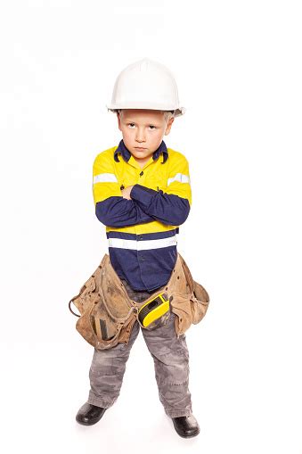 젊은 금발 백인 소년 팔은 노란색과 파란색 하이 비주얼 셔츠 부츠 흰색 하드 모자 도구 벨트 망치 및 테이프 측정에 화가 건설 노동자로 재생 역할을 접힌 가리키기에 대한