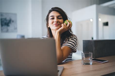 노트북 컴퓨터를 통해 온라인으로 주문하는 사과를 들고 카메라를 바라보는 쾌활한 백인 여성의 절반 길이 초상화 원격 작업을 즐기는 성공적인 여성 프리랜서 사과에 대한 스톡