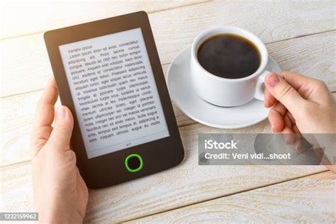 여자 손은 전자 리더와 흰색 나무 테이블 위에 뜨거운 커피 한 잔을 들고 있다 전자책 디스플레이에 공간을 복사합니다 즐거움과 교육을위한 전자 독서 0명에 대한 스톡 사진 및