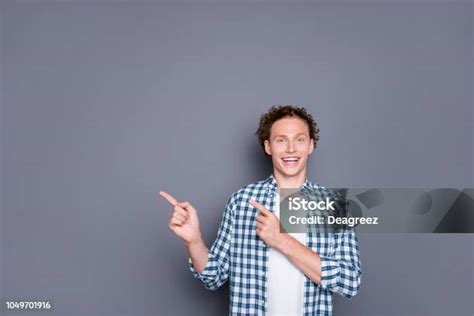 쾌활 한 재미 있는 매력적인 좋은 잘생긴 젊은 남자 캐주얼 체크 무늬 셔츠 물결 모양 머리를 가진 옆을 프로 모션 두 손가락을 가리키는 복사 공간 회색 배경 위에 절연