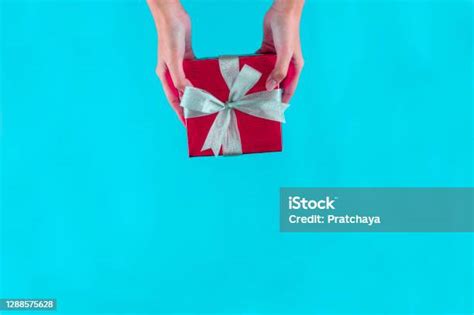 파란색 배경에 리본이 달린 빨간 종이에 싸여 있는 선물 상자를 들고 있는 여성의 손 맨 위 보기입니다 텍스트공간을 복사합니다 휴일 개념 개념에 대한 스톡 사진 및 기타