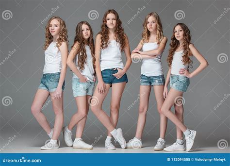 The Fashion Girls Standing Together And Looking At Camera Over Gray