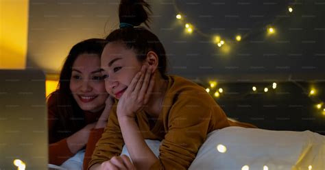 아시아 여자 친구들은 침실의 침대에 누워 노트북 컴퓨터에서 함께 영화나 온라인 쇼핑을 보고 있다 현대 여성 커플은 집에서 함께 기술로 주말 활동 라이프 스타일을 즐긴다