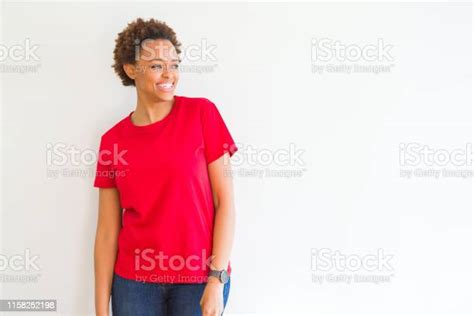 젊은 아름 다운 아프리카 계 미국인 여성 위에 흰색 배경 얼굴에 미소와 함께 옆으로 찾고 자연 스표정 자신감 있게 웃고 있습니다 T 셔츠에 대한 스톡 사진 및 기타 이미지