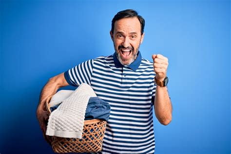 고립된 파란색 배경 위에 옷을 입고 고리버들 바구니를 들고 있는 중년 의자 남자는 자랑스럽고 승리와 성공을 축하하며 매우 흥분하고 환호하는 감정을 축하합니다 가사 집안일에