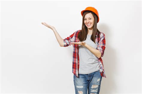 젊은 미소 보호 건설 오렌지에서 아름 다운 여자 옆으로 흰색 배경에 고립 된 복사 공간에 가리키는 손 헬멧 재건축 아파트 룸 악기입니다 수리 가정 개념입니다 Diy에 대한