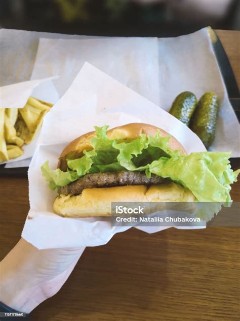 양상추 잎을 가진 패스트 푸드 카페 중간 로스트 고기 패티 플라스틱 용기에 양상추 옆에 토마토를 종이 공예 포장에 여자 손을 들고 햄버거 건강에 해로운 다이어트 식품
