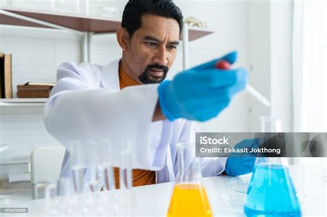 흰색 실험복을 입고 파란색 고무장갑을 낀 남자 교사가 선반과 탁자 위에 많은 실험 도구를 올려놓았다 오른손에 있는 피펫을