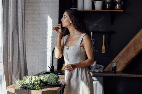 Attractive Young Woman Is Happily Eating Leaf Of Greenery In Kitchen