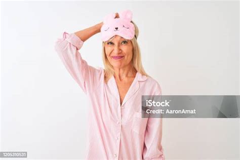 고립된 흰색 배경 위에 수면 마스크와 잠옷을 입은 중년 여성이 혼란스럽고 질문에 대해 궁금해합니다 의심의 여지가 머리에 손으로 생각 펜시브 개념 개념에 대한 스톡 사진 및