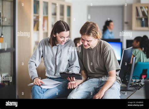 High Babe Babes Sharing Digital Tablet While Sitting On Desk In Computer Lab Stock Photo