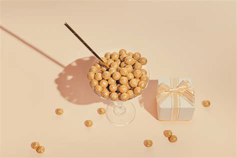 현재 상자로 만든 창의적인 구성으로 활 장식적인 황금 공 파스텔 베이지 배경의 짚이 있는 마티니 글래스 축제와 파티 개념 최소한의 스타일 0명에 대한 스톡 사진 및 기타