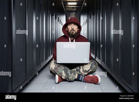 the hacker in a hood sits with the computer among servers the burglar