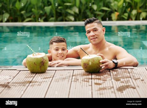 Father And Preteen Son Spending Time In Swimming Pool And Enjoying Refreshing Coconut Cocktails