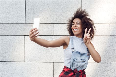 행복 카메라에 승리 제스처를 보여주는 스마트 폰에 셀카를 복용 회색 벽에 고립 된 도시 거리에서 젊은 여자 갈색 머리에 대한 스톡 사진 및 기타 이미지 Istock
