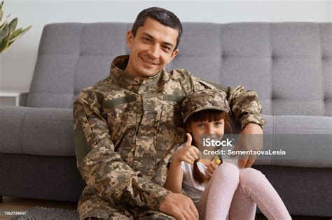 군대 후 집으로 돌아오는 위장 유니폼을 입고 딸과 함께 시간을 보내고 행복한 표정으로 카메라를 보고 엄지 손가락을 드러내는 아이의 미소 가 2명에 대한 스톡 사진 및 기타