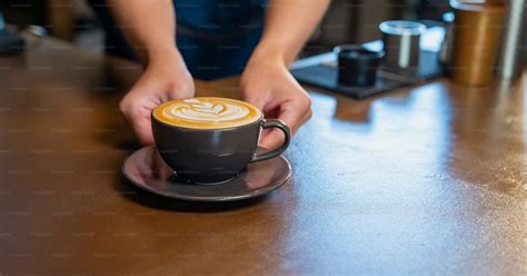 아시아 남자 바리 스타는 카페의 바 카운터에서 고객에게 커피 컵에 뜨거운 커피 라떼를 만들고 있습니다 남성 커피 숍 웨이터는