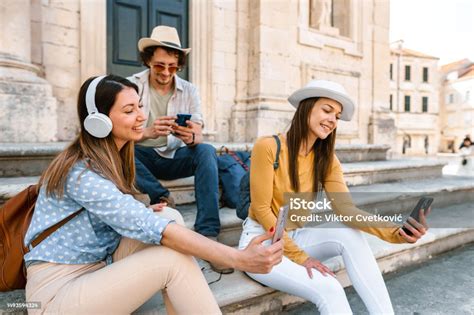도시 광장의 계단에 앉아 화상 통화로 이야기하는 세 명의 웃는 관광객 20 24세에 대한 스톡 사진 및 기타 이미지 20 24세 25 29세 3 명 Istock