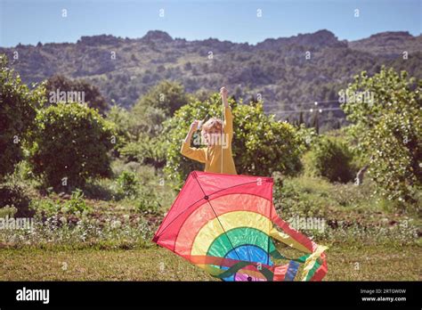 Cheerful Boy Pulling Fallen On Grass Kite In Summer Day On Green Light