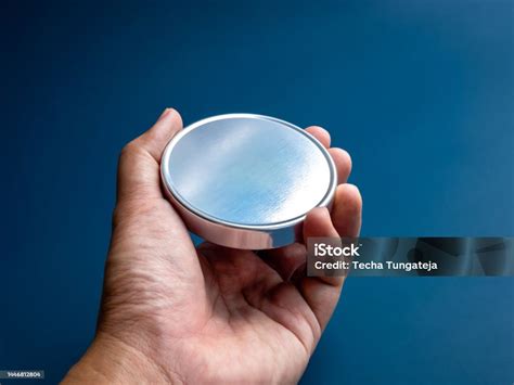 파란색 배경에 격리된 빈 빈 스테인리스 스틸 배지 둥근 모양을 들고 있는 클로즈업 손 원형 모양 은색 및 금속 질감의 금속 버튼 원형 크롬 알루미늄 플레이트 강철에 대한