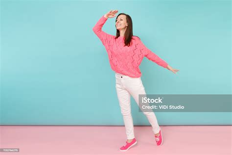 니트 로즈 스웨터 스튜디오에서 밝은 분홍색 파란색 파스텔 벽 배경에 고립 된 포즈 흰색 바지에 웃는 젊은 여자의 전체 길이 초상화 패션 라이프 스타일 개념입니다 복사 공간을