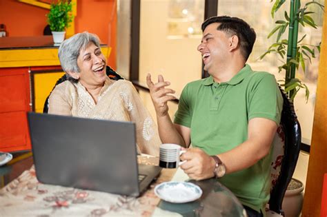 젊은 인도 아들과 늙은 어머니가 웃으며 노트북을 사용하거나 함께 영화를 보고 젊은 세대는 노인과 시간을 보내고 집에서 엔터테인먼트와 재미를 느낀다 2명에 대한 스톡 사진 및