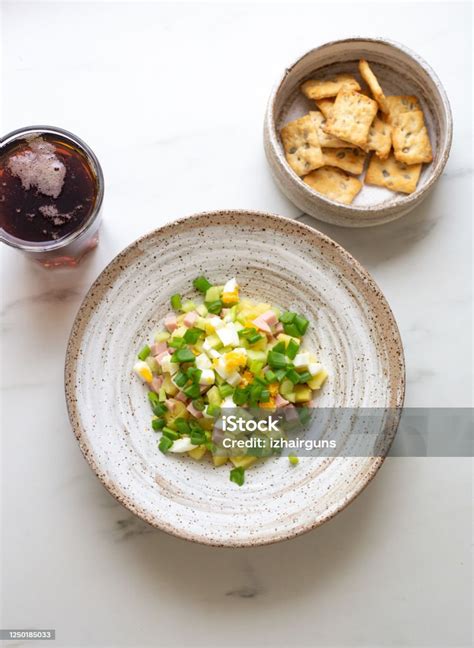 삶은 채소와 소시지의 샐러드 올리비에와 마요네즈를 그릇에 넣고 가벼운 나무 배경 위에 있습니다 가벼운 배경에 러시아어 새해 또는 크리스마스 샐러드 러시아식 샐러드에 대한