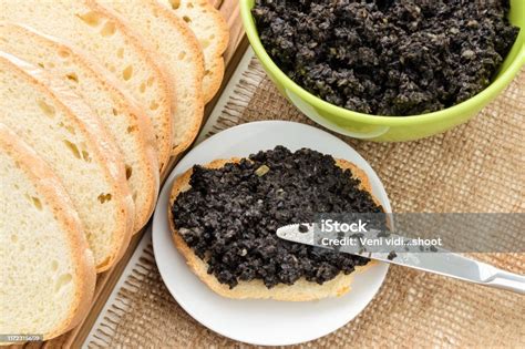 타파네이드 샌드위치와 테이블 나이프를 소저에 얹고 신선한 태피네이드가 있는 녹색 그릇에 삼베 테이블 냅킨에 얇게 썬 밀 빵을 얹습니다 멸치 마늘 올리브 오일을 곁들인 홈