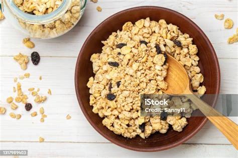 건강한 아침 식사 흰 나무 테이블에 점토 그릇에 말린 포도를 곁들인 뮤즐리 뮤즐리는 테이블에 흩어져 있습니다 텍스트 공간입니다 아침식사 시리얼에 대한 스톡 사진 및 기타