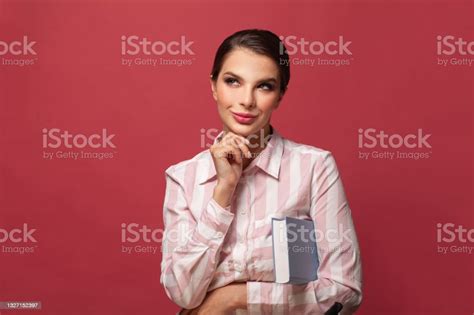 빨간 벽 배경 스튜디오 초상화에 고립 된 포즈를 취하는 책을 들고 미소 짓는 젊은 갈색 머리 여성 복사 공간을 모의합니다