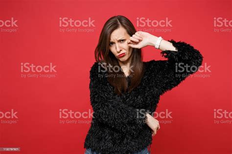 검은 모피 스웨터 서 서와 스튜디오에서 밝은 붉은 벽 배경에 고립 된 눈물을 닦아 젊은 여 자가 우는 화가의 초상화 사람들은 진심으로 감정 라이프 스타일 개념입니다 복사