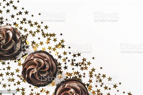 초콜릿 아이싱과 황금 별 모양의 색종이와 흰색 배경에 금 빛을 뿌린 초콜릿 컵 케이크 휴일 개념입니다 디자인에 대한 모형 플랫 레이 스타일입니다 공간을 복사합니다 0명에