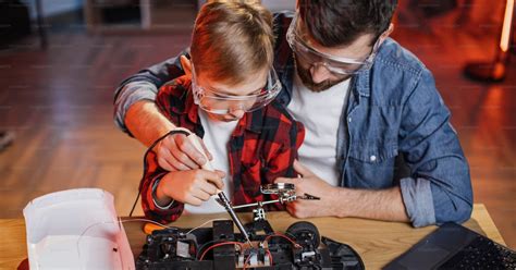 집에서 빨간 장난감 자동차를 수리하기 위해 납땜 인두를 사용하는 보호 안경을 쓴 아들과 함께하는 아버지 유지 보수 가족 및 공생의 개념 사진 Unsplash의