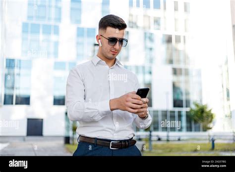 A Man Wearing A White Shirt Is Focused On His Cell Phone Screen Scrolling Or Typing While