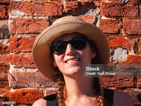 붉은 벽돌 벽에 밀짚모자를 쓴 젊은 여자 도시 배경 예쁜 밀레니얼 세대 소녀가 여름 도시 거리를 걷는다 땋은 머리에 대한 스톡