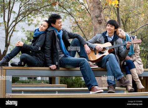 Two Couples Sit On A Park Bench And Listen To A Friend Play Guitar