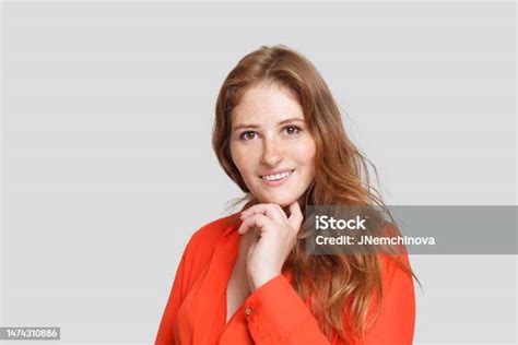 빨간 블라우스를 입고 흰색 스튜디오 벽에 포즈를 취하는 생강 머리와 주근깨가 있는 얼굴을 가진 매력적인 젊은 여성의 실내 초상화 30 34세에 대한 스톡 사진 및 기타