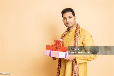 베이지색 배경에 고립된 디왈리 축제를 축하하는 빨간 선물 상자를 들고 전통 옷을 입은 행복한 젊은 잘생긴 인도 남자 남자에 대한 스톡 사진 및 기타 이미지 Istock
