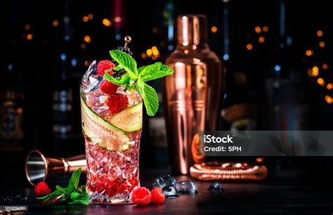 드라이 진 강장제 시럽 리치 주스 레몬 라즈베리 얇게 썬 오이 얼음을 곁들인 블랙베리를 곁들인 로즈 가든 칵테일 음료 검은색 바 카운터 배경 바 도구 및 병 Gin